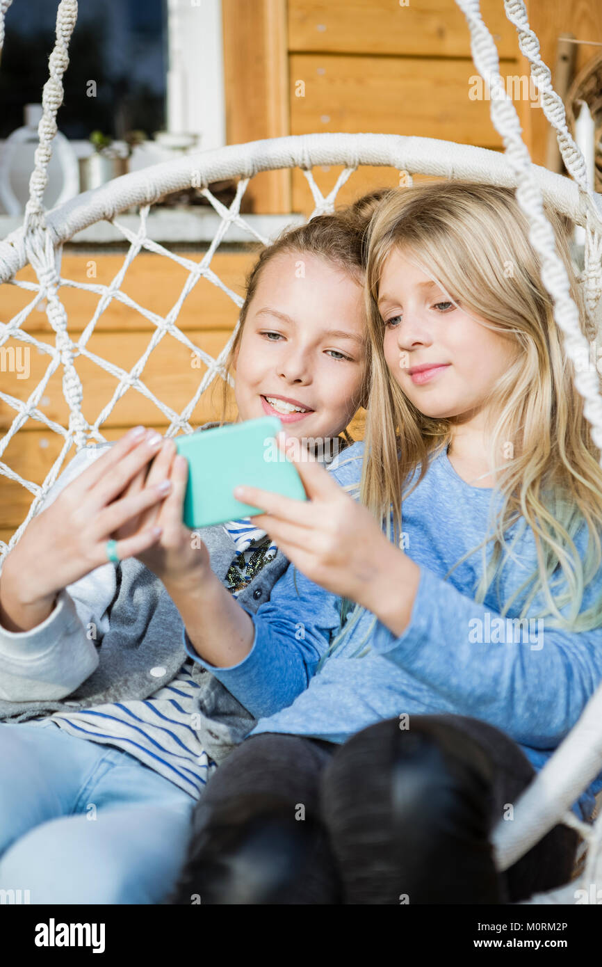 Portrait of two girls relaxing in a hanging chair taking selfie with ...