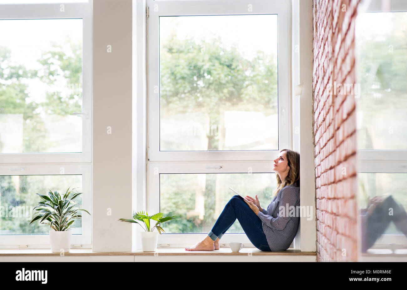 Woman sitting at home on the window sill, reading a book Stock Photo ...