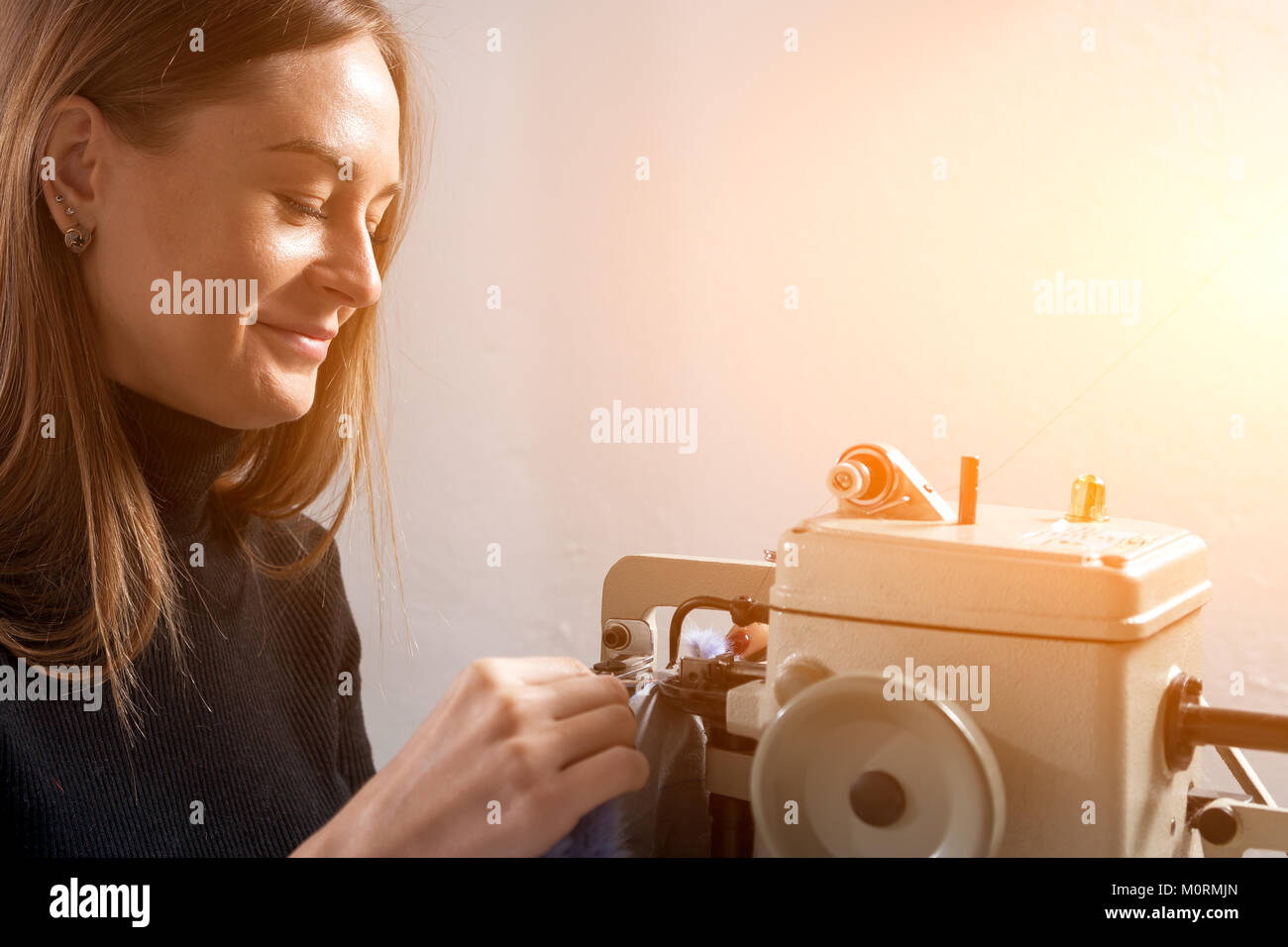 A young cheerful woman furrier smiles and sews a bright fur coat of ...