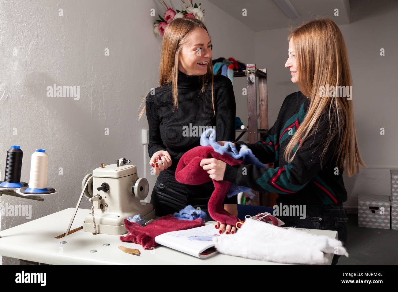 Two young women furriers smiles and advise how to properly sew a fur ...