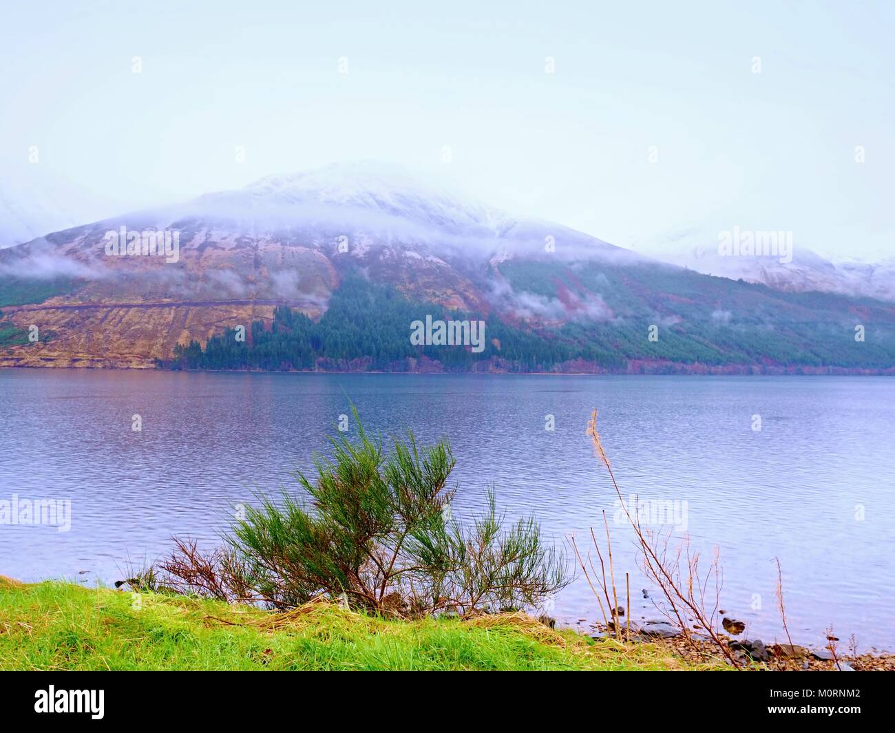 Spring landscape with snowy mountains and lake. Low clouds bring snow ...