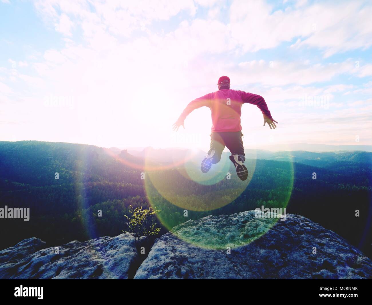 Jumping man. Young crazy man is jumping on rocky summit above landscape ...