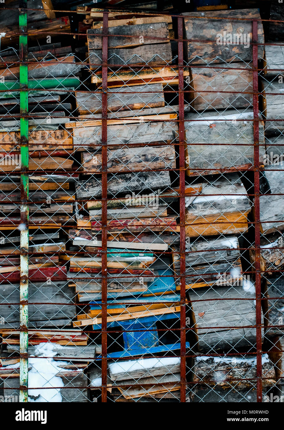 A stack of colored wood and planks for rustic oven hidden behind wire ...