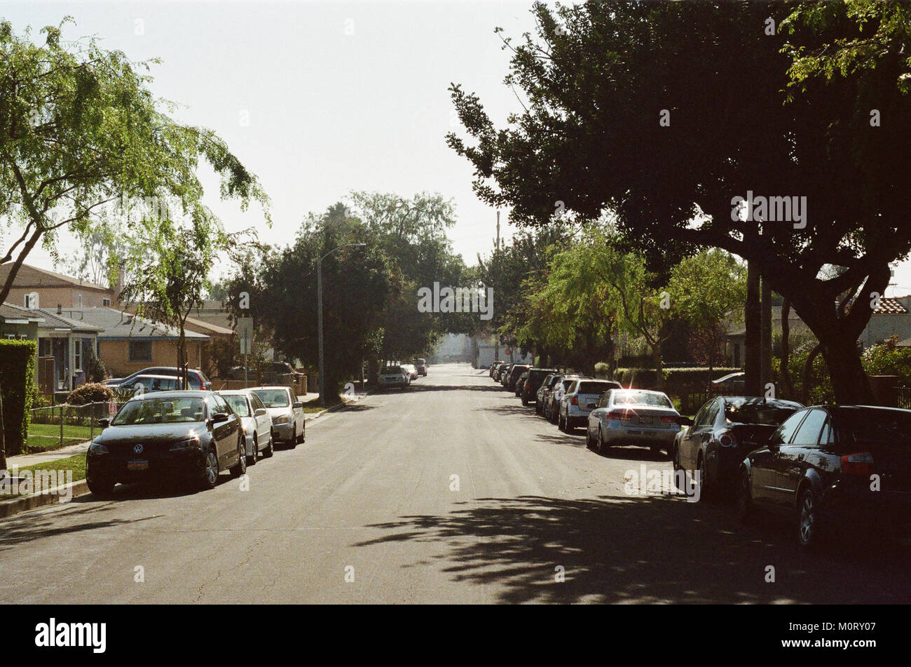 This image depicts a street in a village with cars parked along the ...