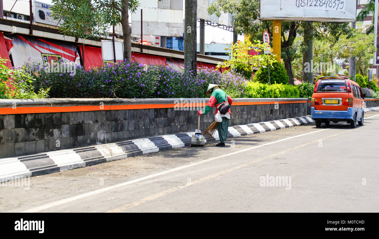 A worker cleans up trash from the street. Samarang, Java, Indonesia ...