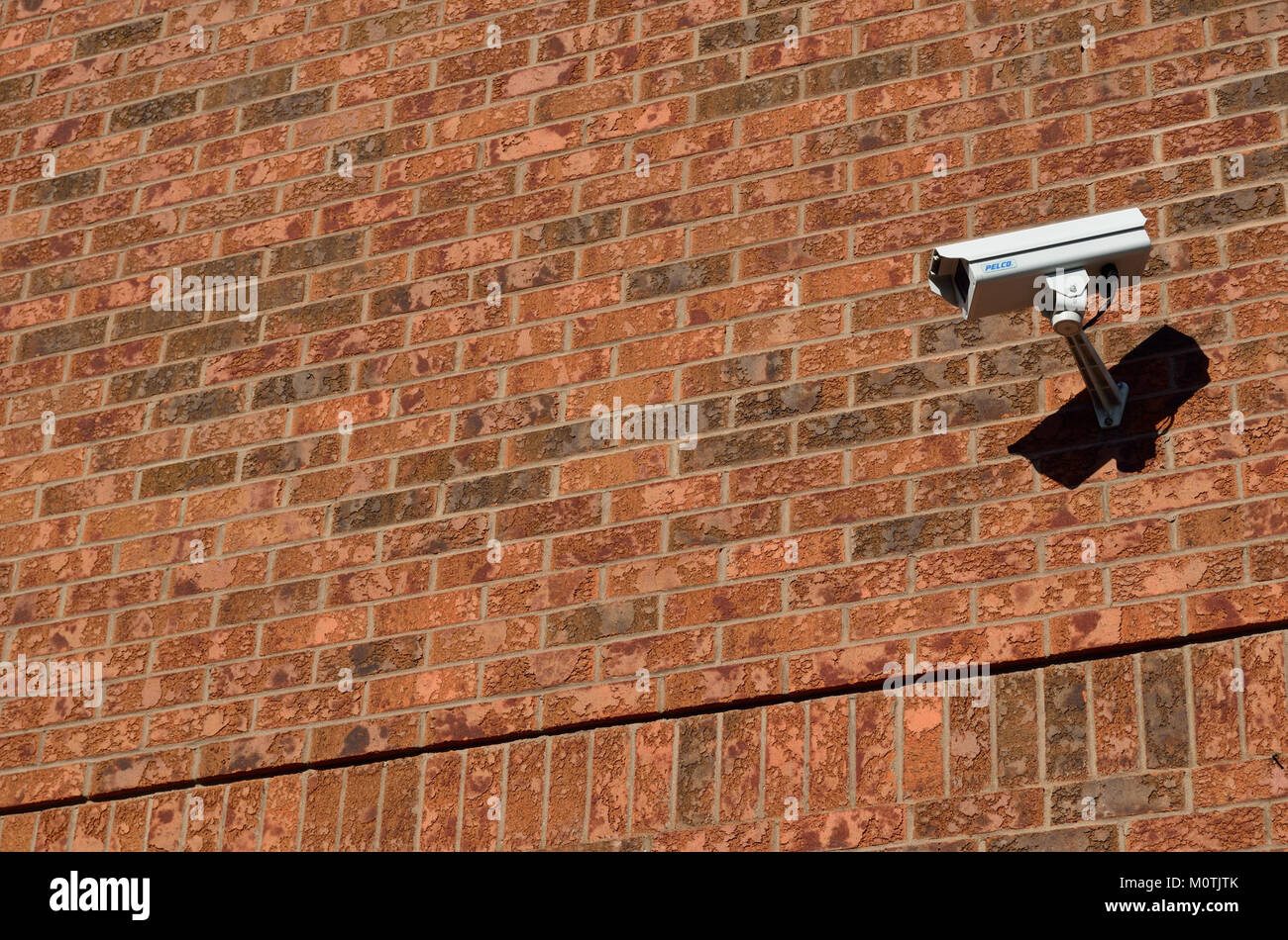 The image shows a CCTV camera mounted on a brick wall, often used for ...