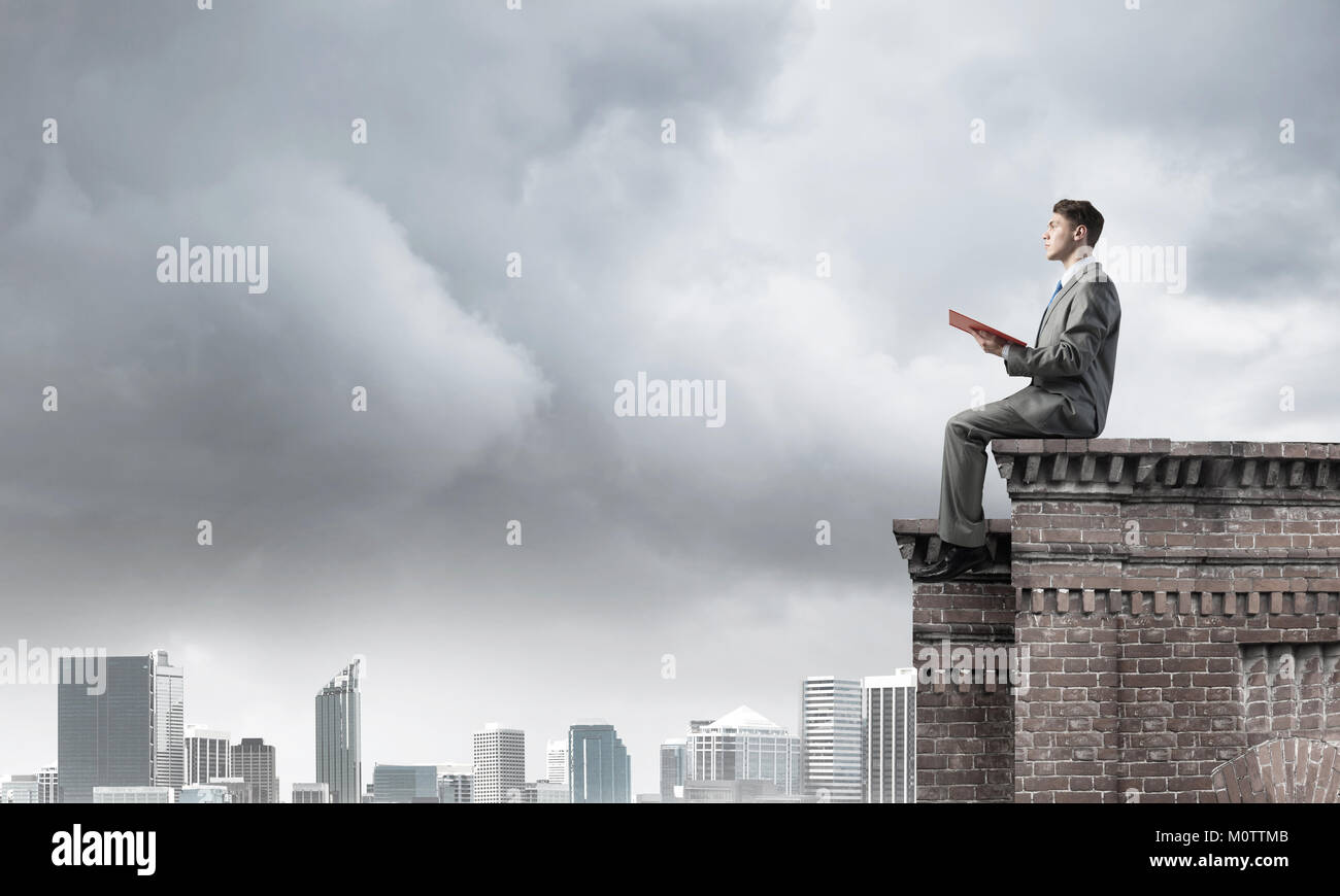 Man on roof edge reading book and cityscape at background Stock Photo ...