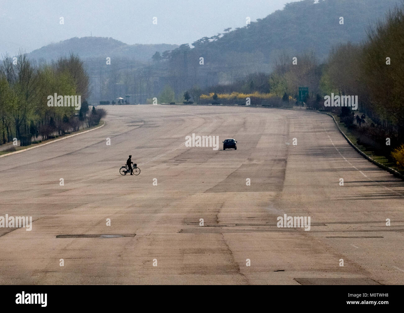North Korean man with a bicyle crossing an empty highway in North Korea ...
