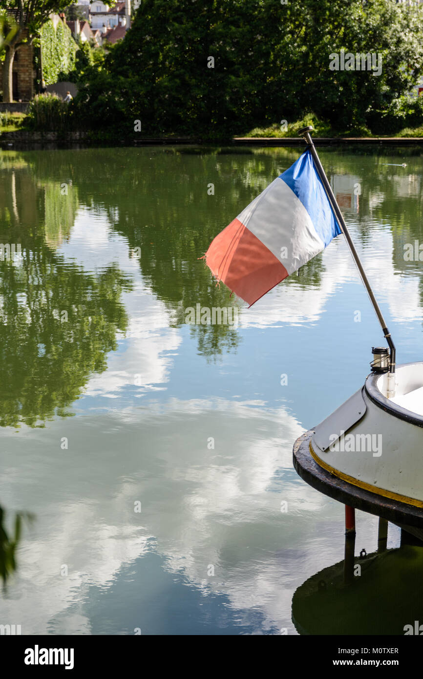 French flag flying in the wind at the stern of a riverboat over still ...