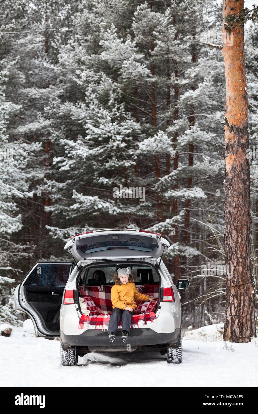 Smiling young girl resting in car back boot for luggage. Winter ...