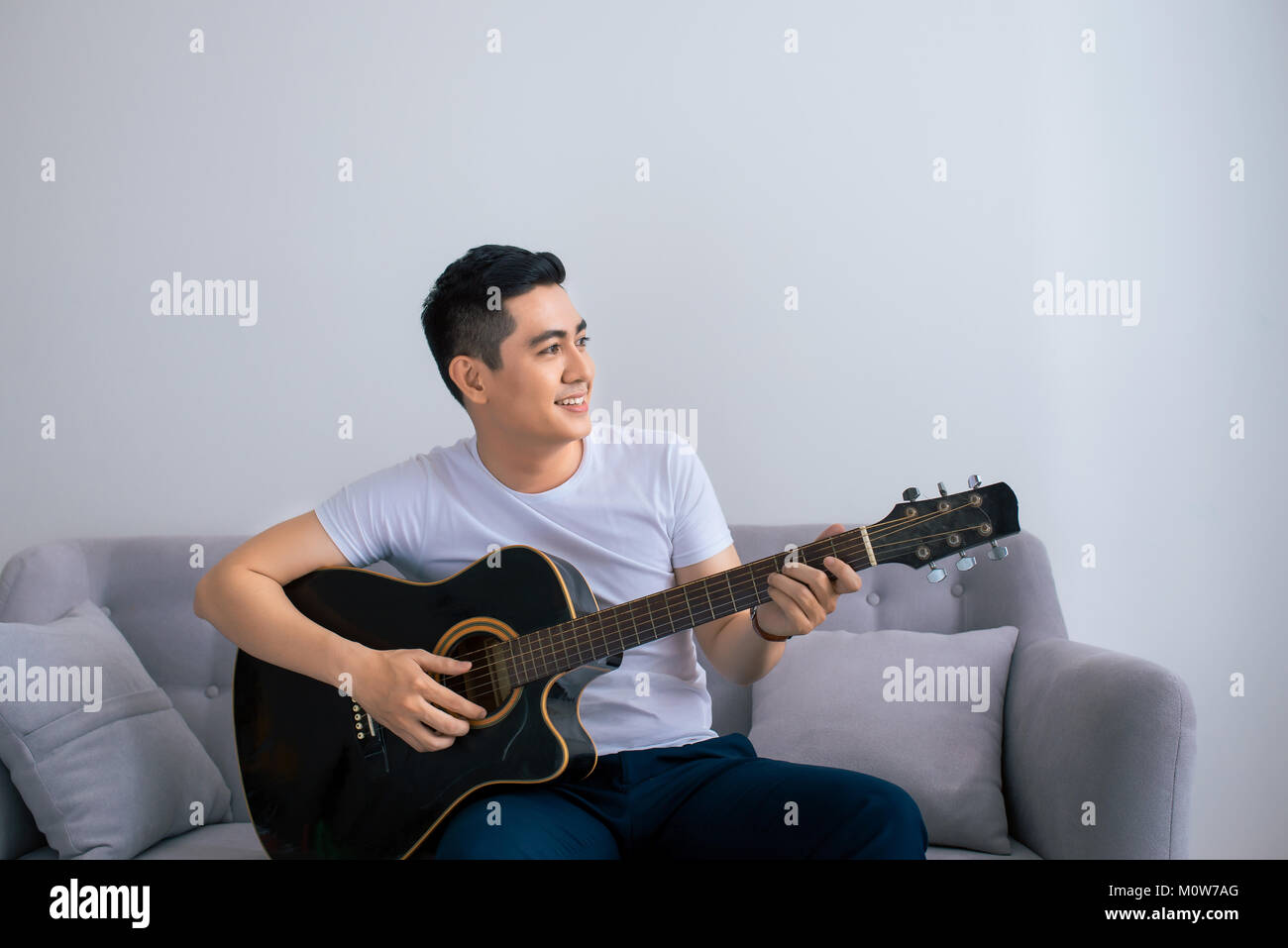 Handsome asian man playing on the guitar on the couch at home Stock ...