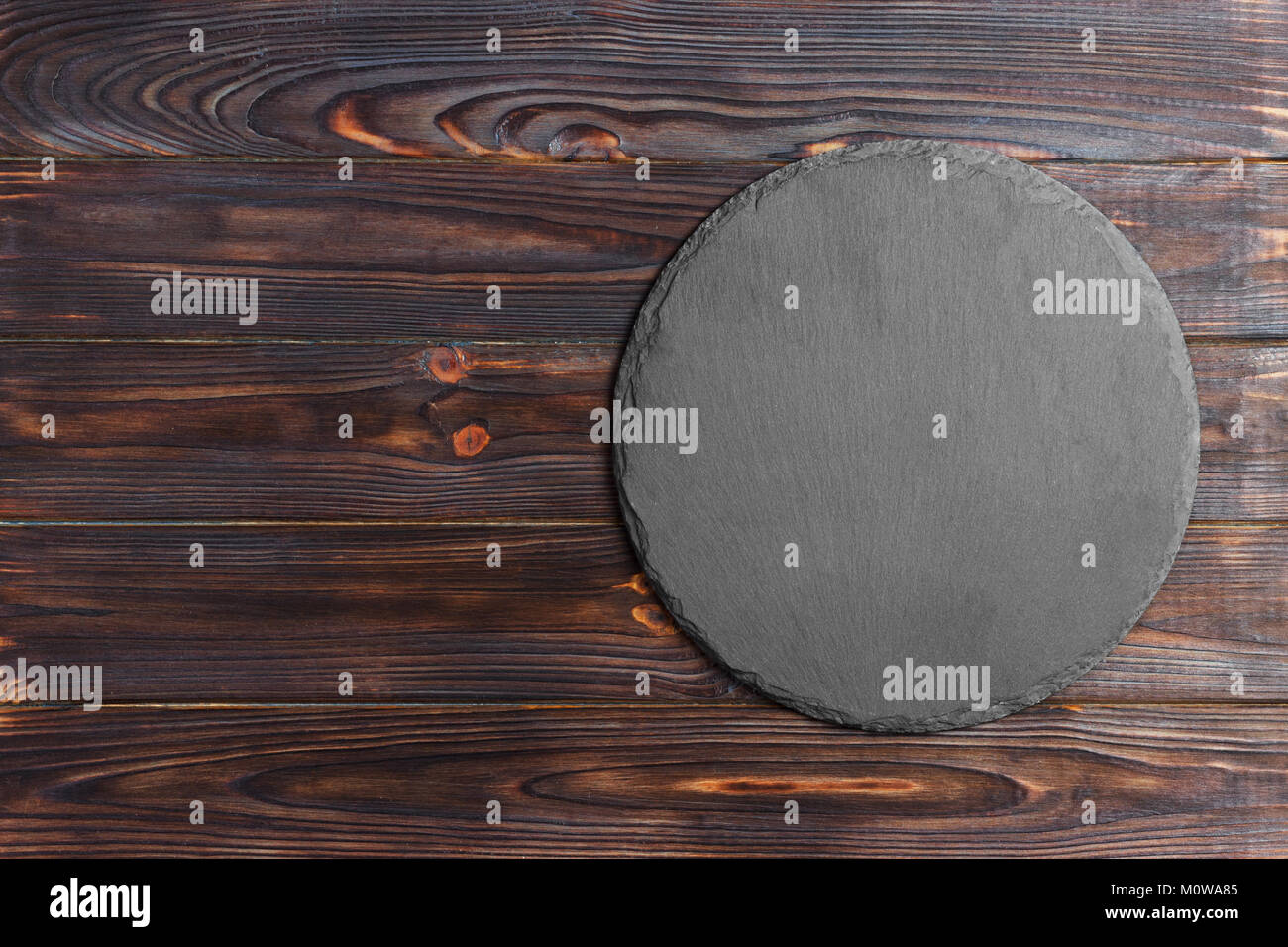 Round natural slate board. Dark gray slate stand on wooden background ...