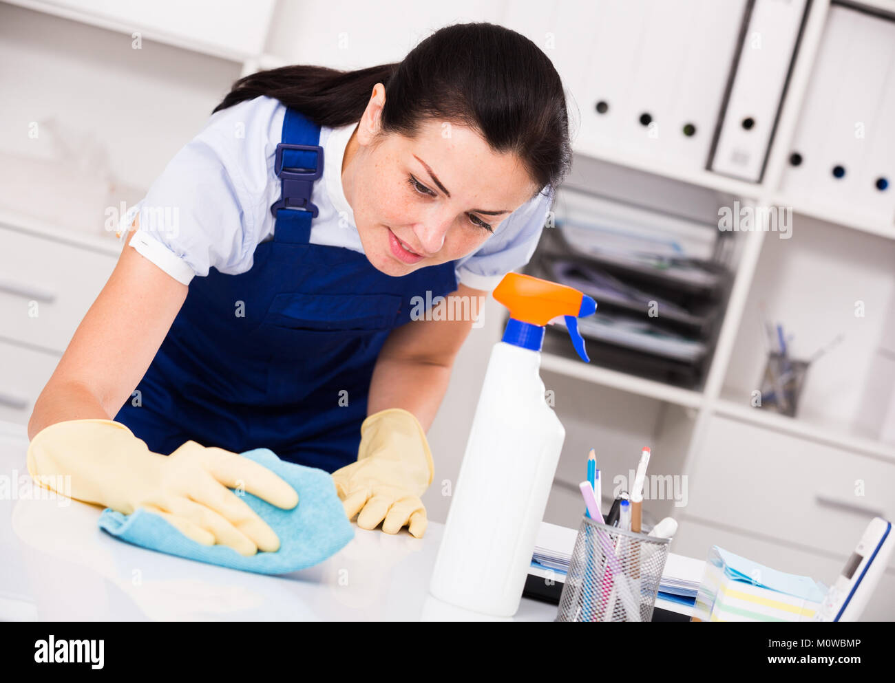 Portrait of adult female cleaning office table with rag and cleanser ...