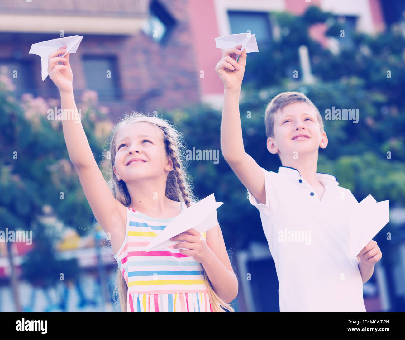 two glad children playing with paper planes in town on summer day Stock ...