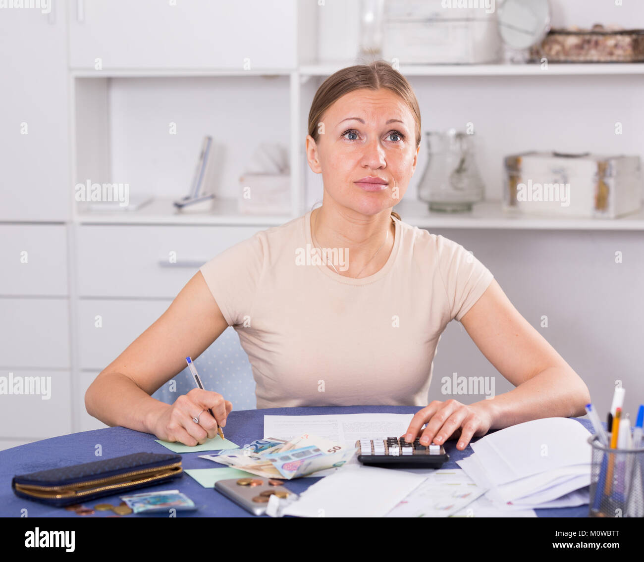 Woman sitting at table at home with calculator counting money for ...