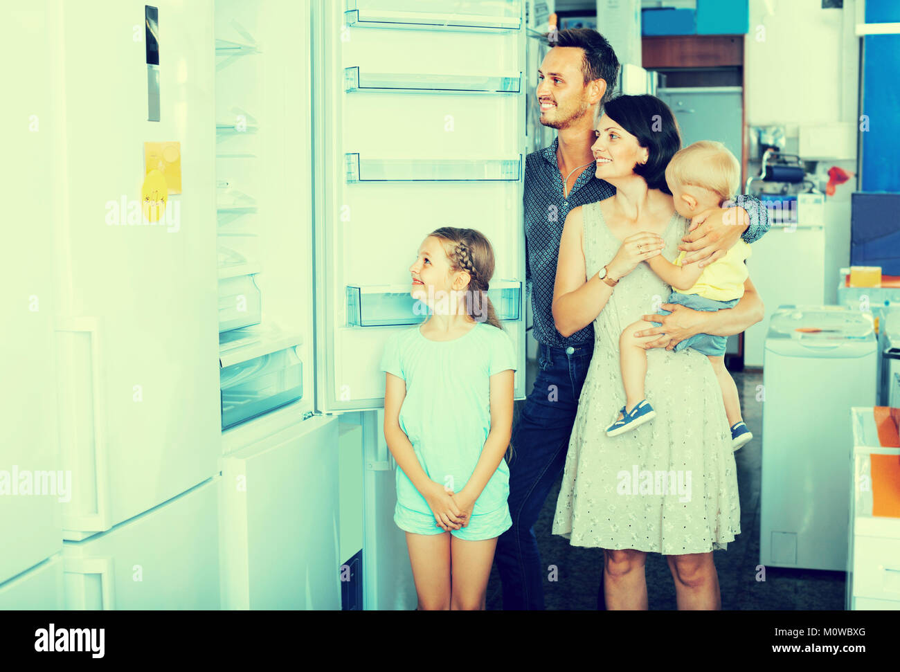 smiling family with two children choosing new fridge in household store ...