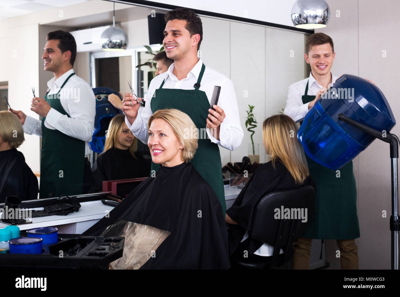 Happy professional stylist cutting hair of elderly blonde in salon ...