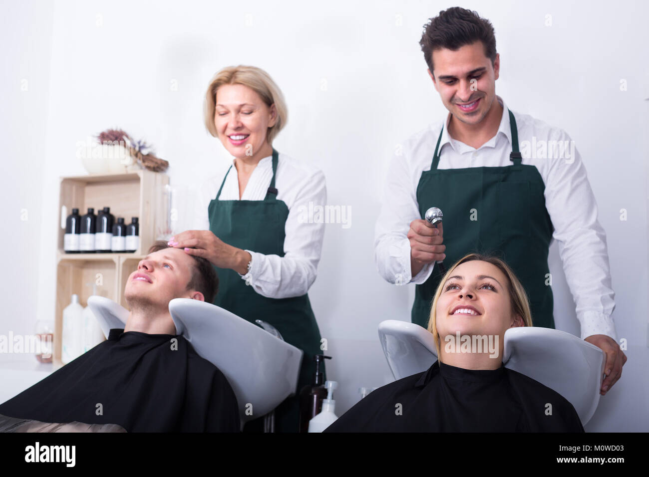 Two positive smiling hairdressers washing hair of clients at salon ...