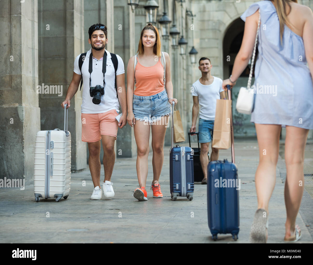 Happy people tourists taking walk and dragging luggage in town on ...