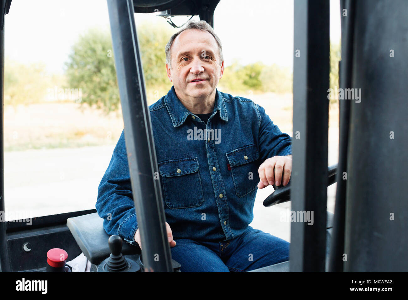 Diligent positive glad elderly man of winery goes on loader Stock Photo ...