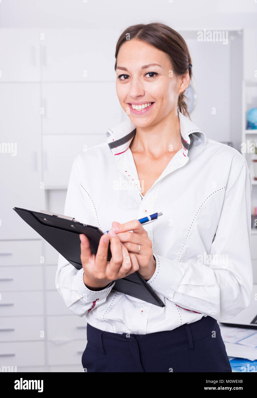smiling business female employee holding clipboard in hands in firm ...