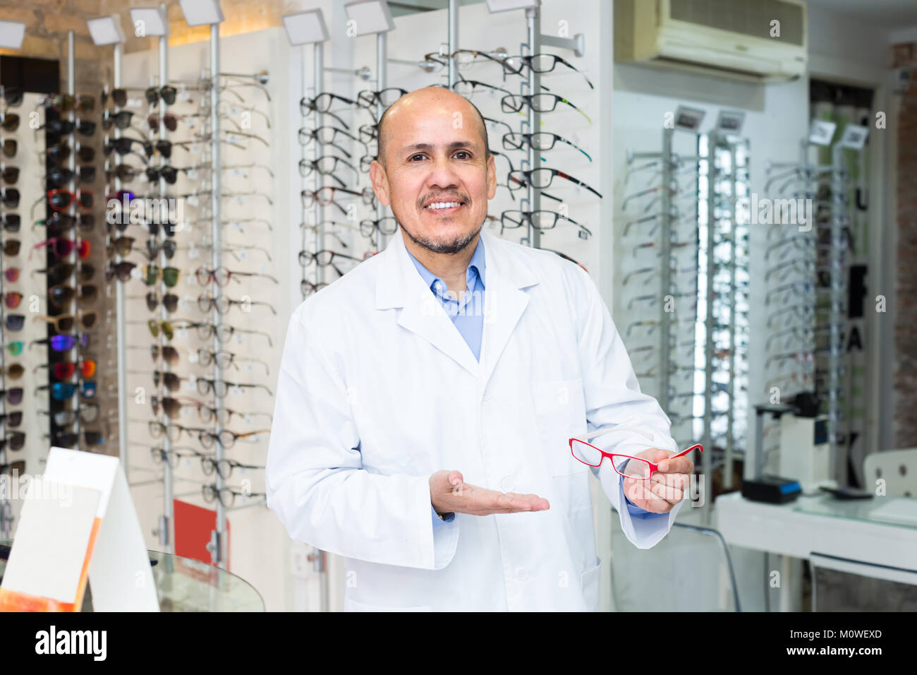 Friendly smiling professional male optician posing near stand with ...