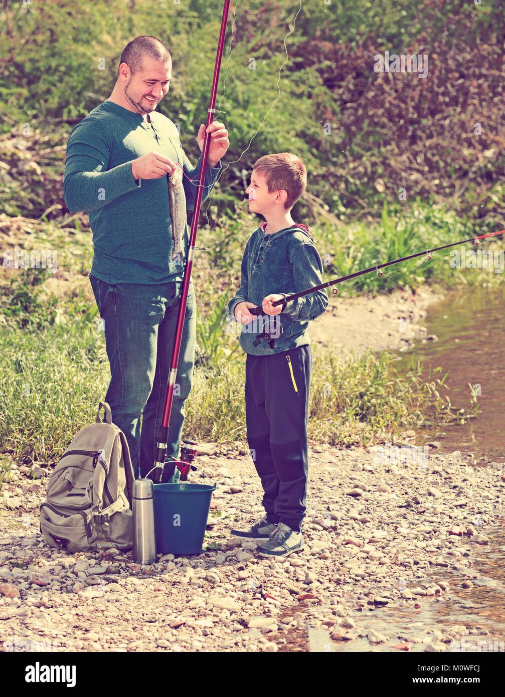 Portrait of happy friendly glad smiling father and cute son fishing ...
