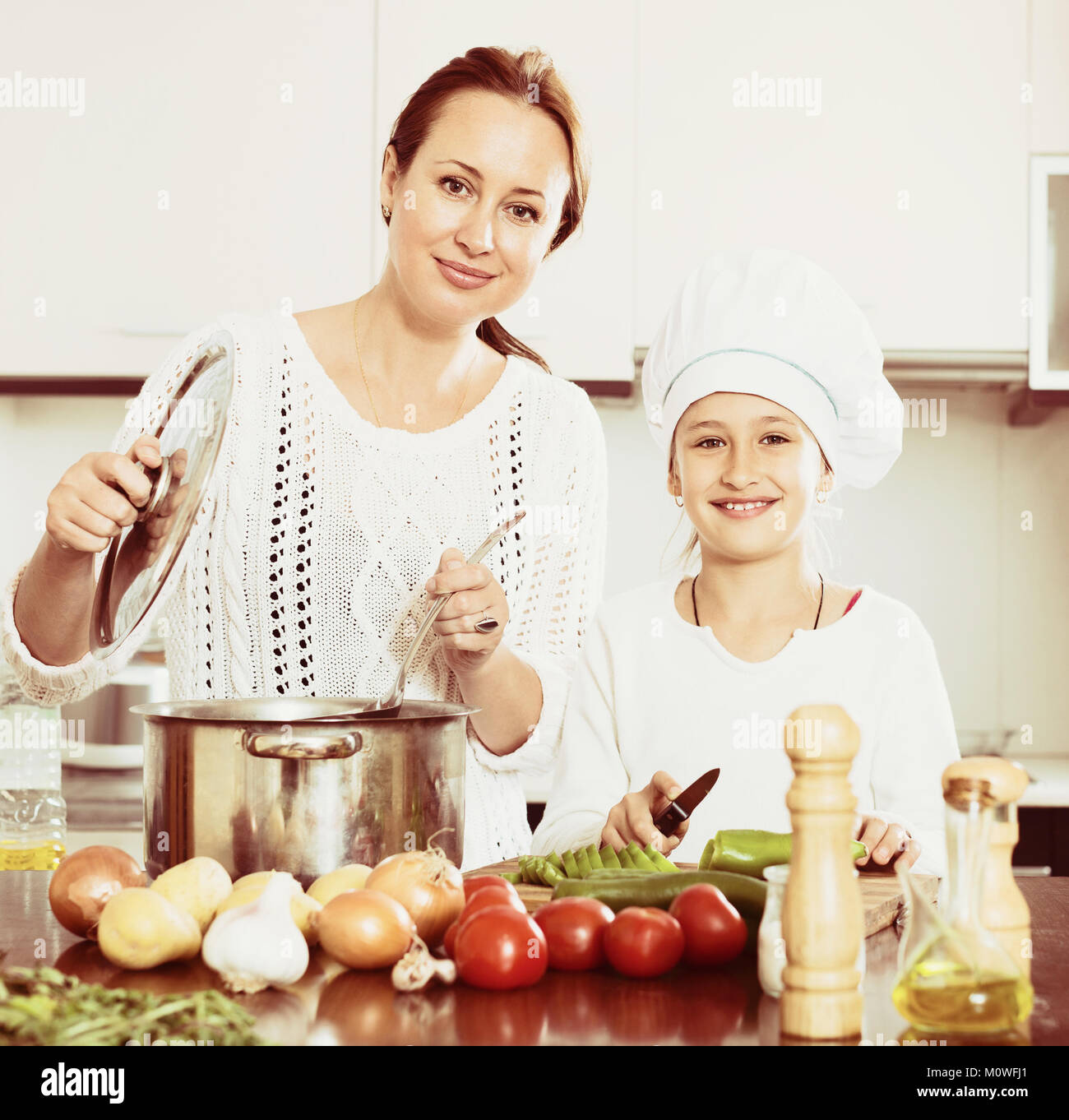 Happy little girl and her mother cook soup together in the kitchen ...