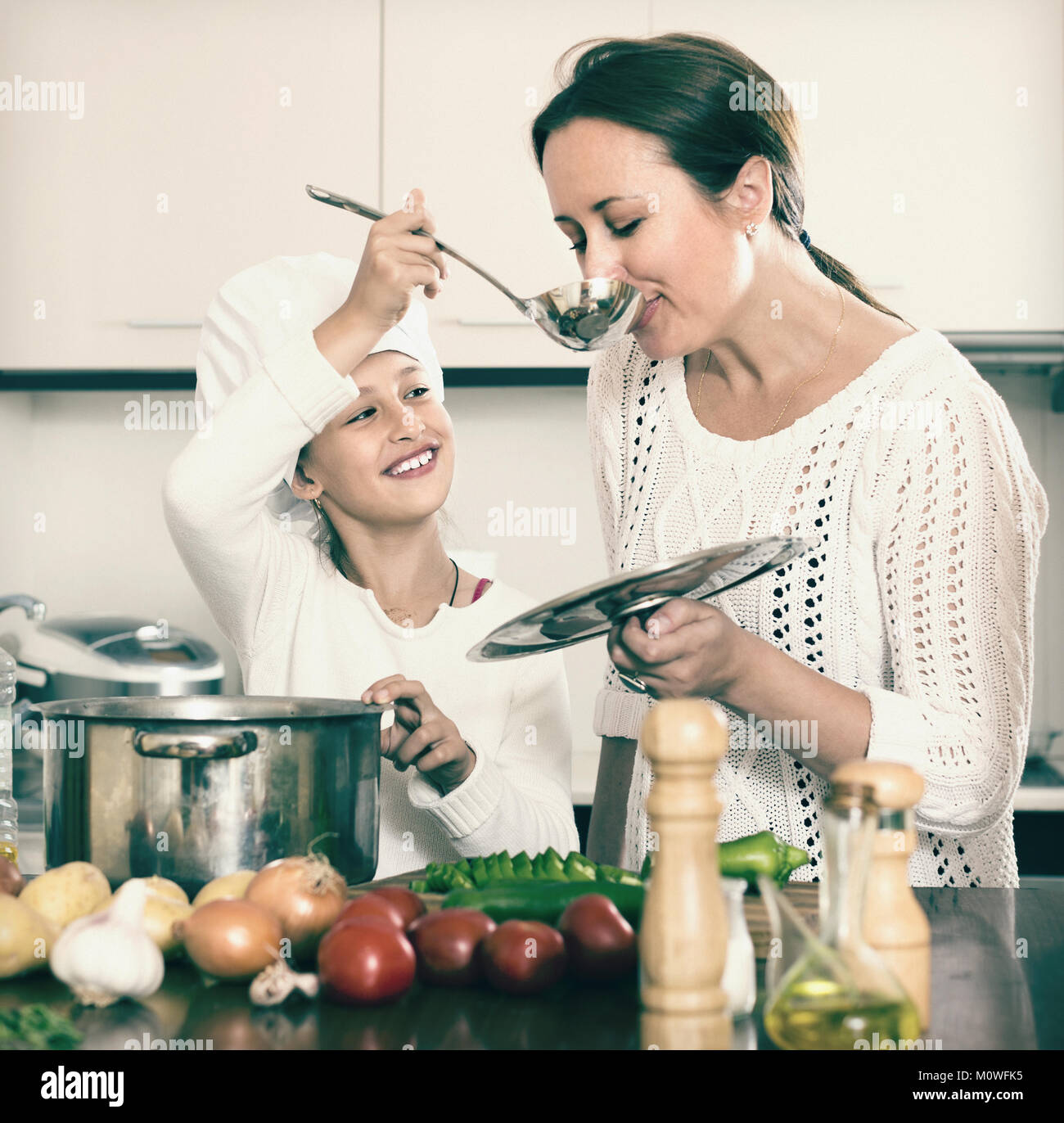 Smiling mother and her cheerful daughter preparing soup at kitchen ...