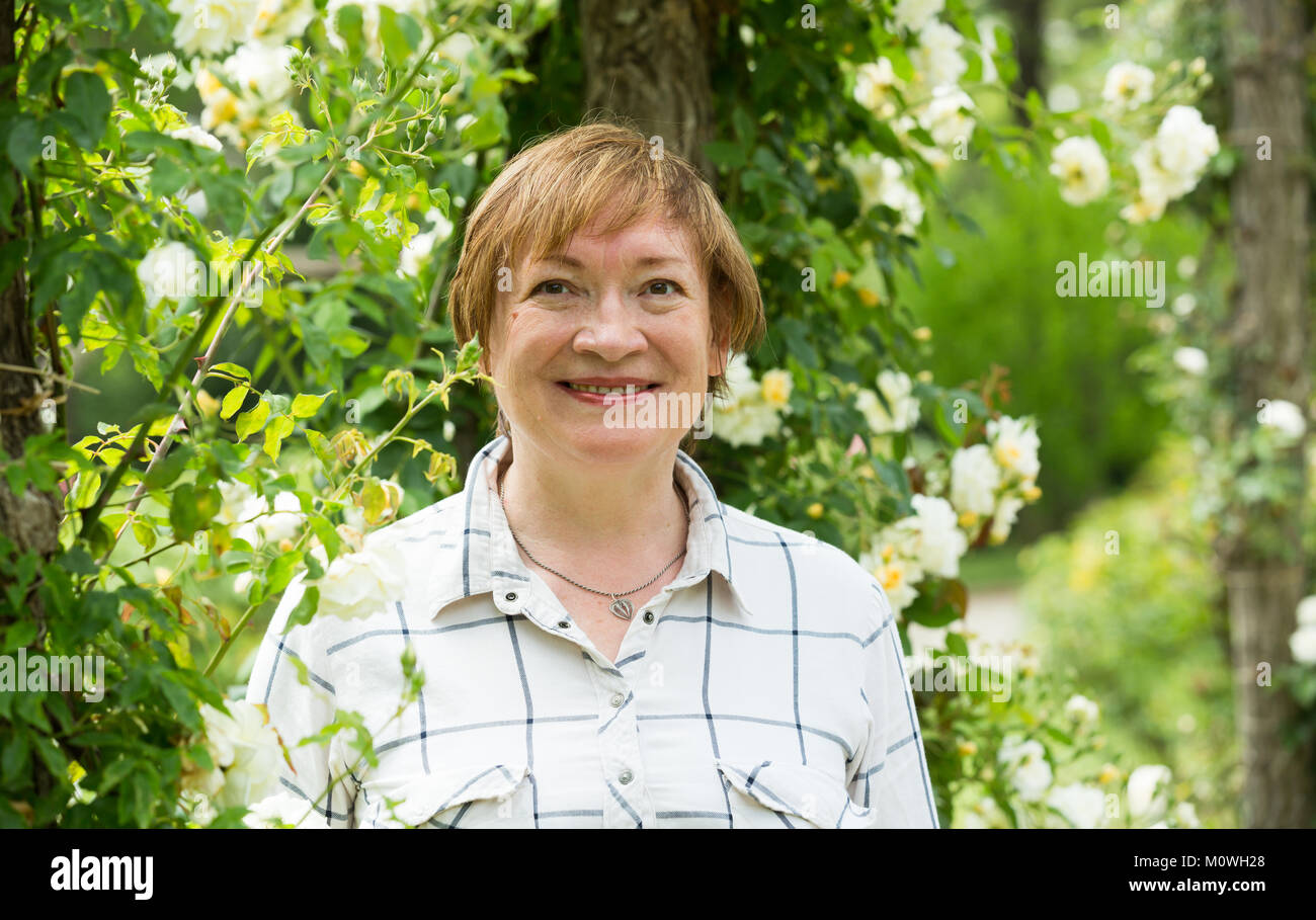 Portrait of cheerful retiree woman standing outdoors in fine weather ...