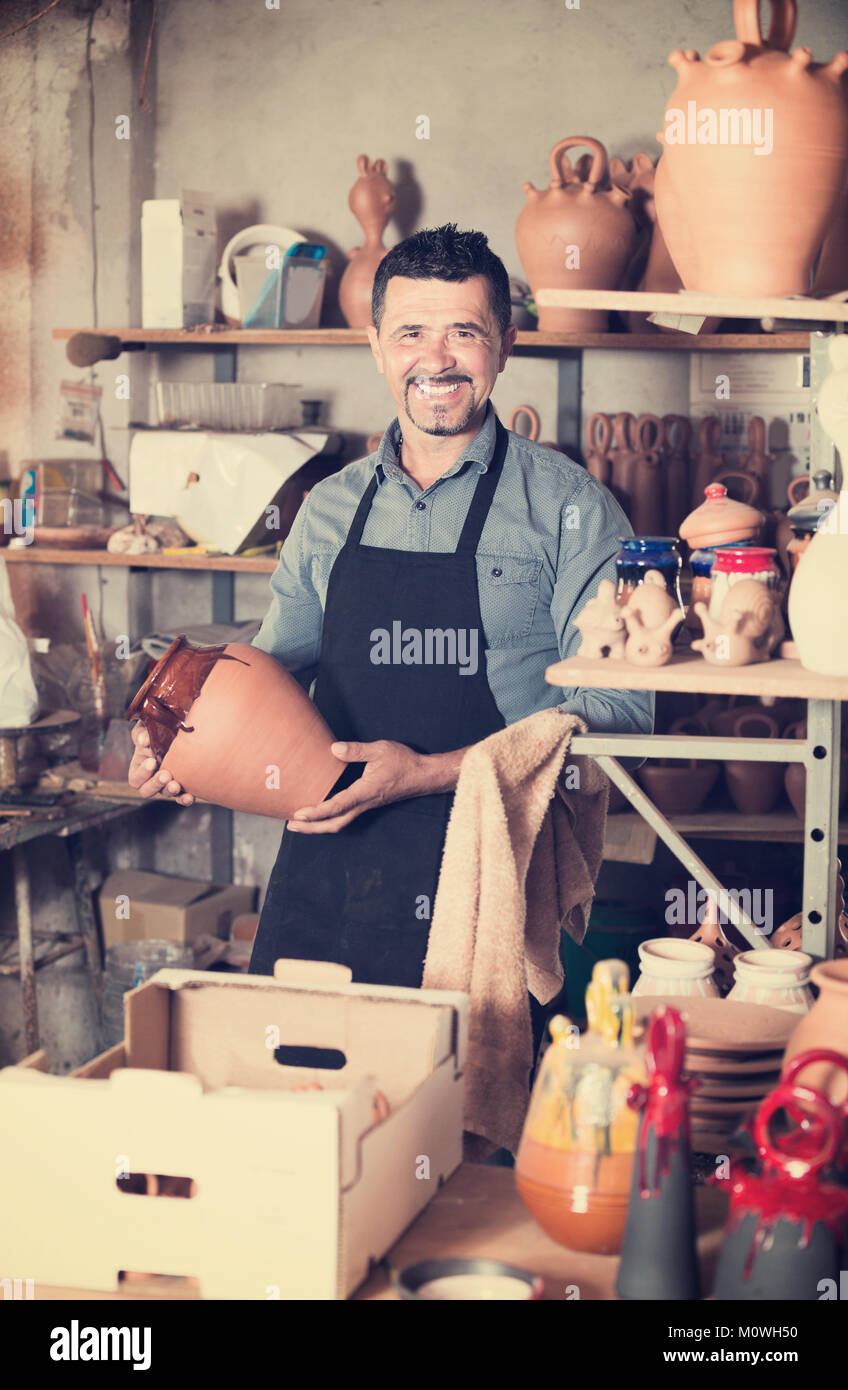 Portrait of glad craftsman with ceramic crockery in hands in studio ...