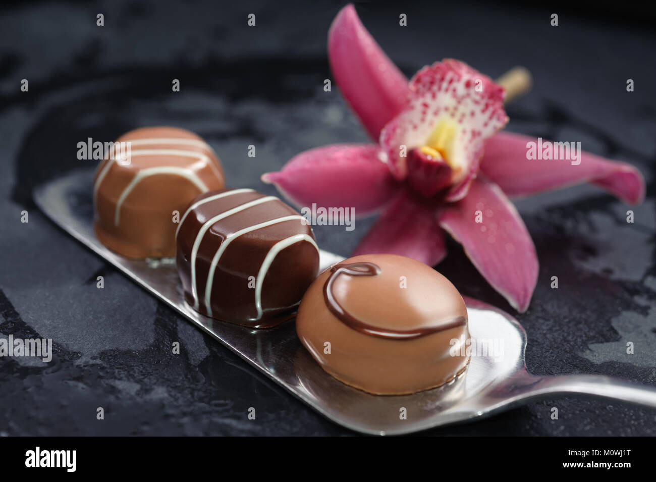 Chocolate pralines and orchid flower on black stone surface Stock Photo ...