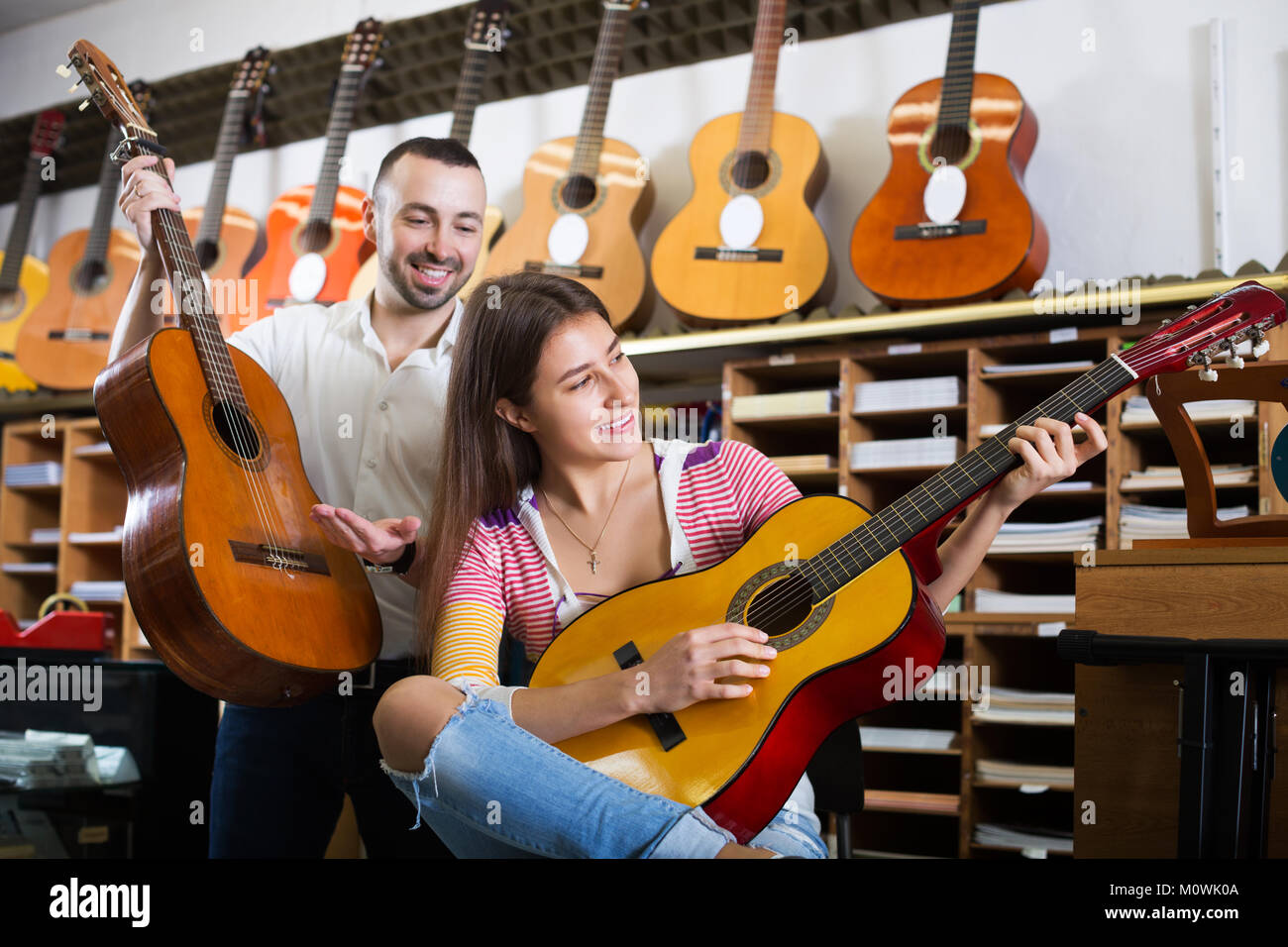 Positive girl and handsome guy playing the guitars in shop Stock Photo ...