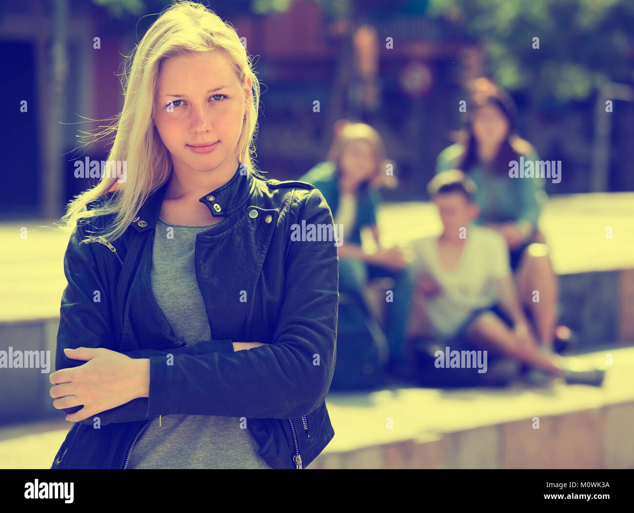 Portrait of sad outcasted teenager girl being mobbed by other teenagers ...