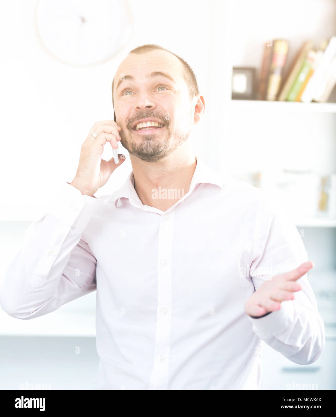 Positive young man texting and calling by smartphone at his workplace ...