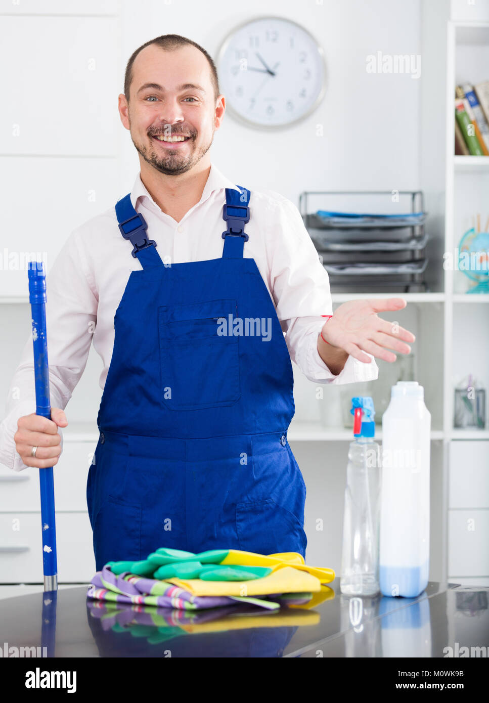 Positive young man in apron cleaning his office desk by cleanser Stock ...
