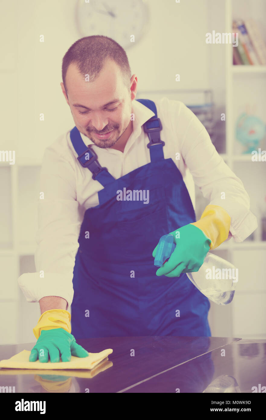 Positive young man in apron cleaning his office desk by cleanser Stock ...