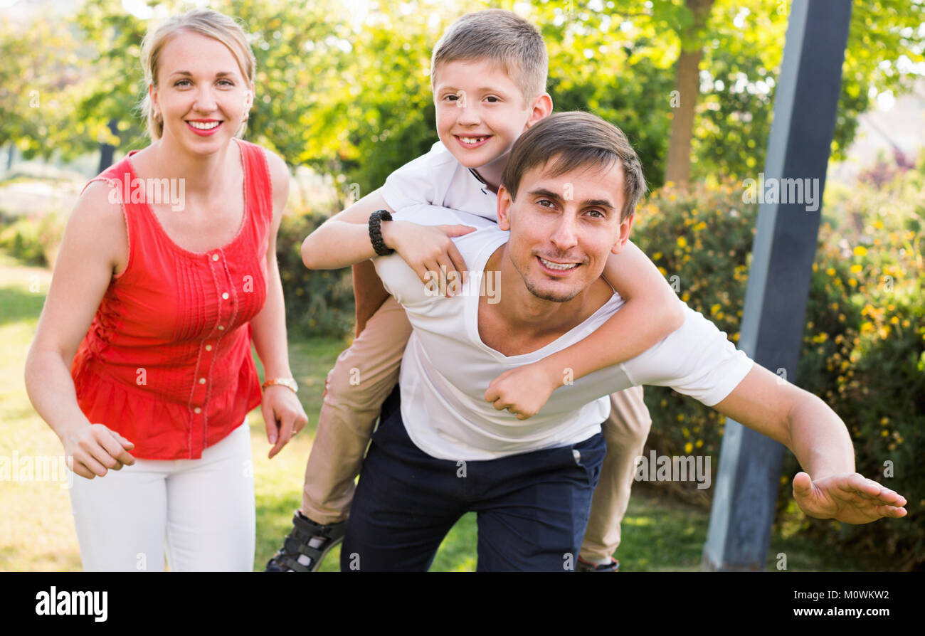 Portrait of cheerful family with boy sitting on father's back hugging ...