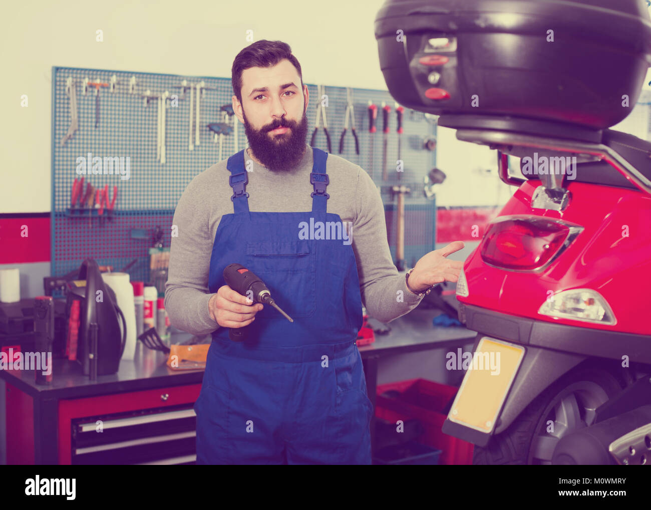 Positive man worker repairing motorcycle in workshop Stock Photo - Alamy
