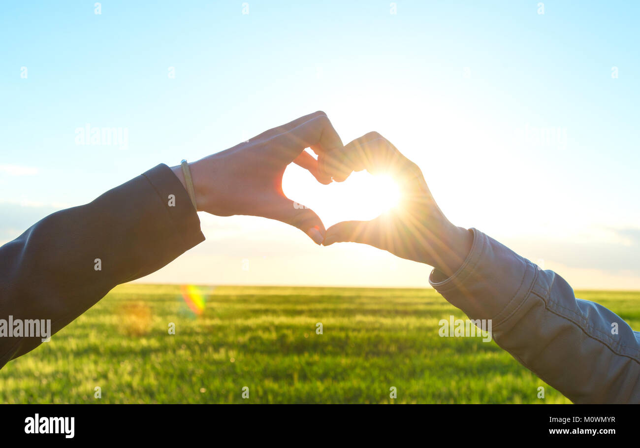Romantic couple in love gesturing a heart with fingers on the sunset ...