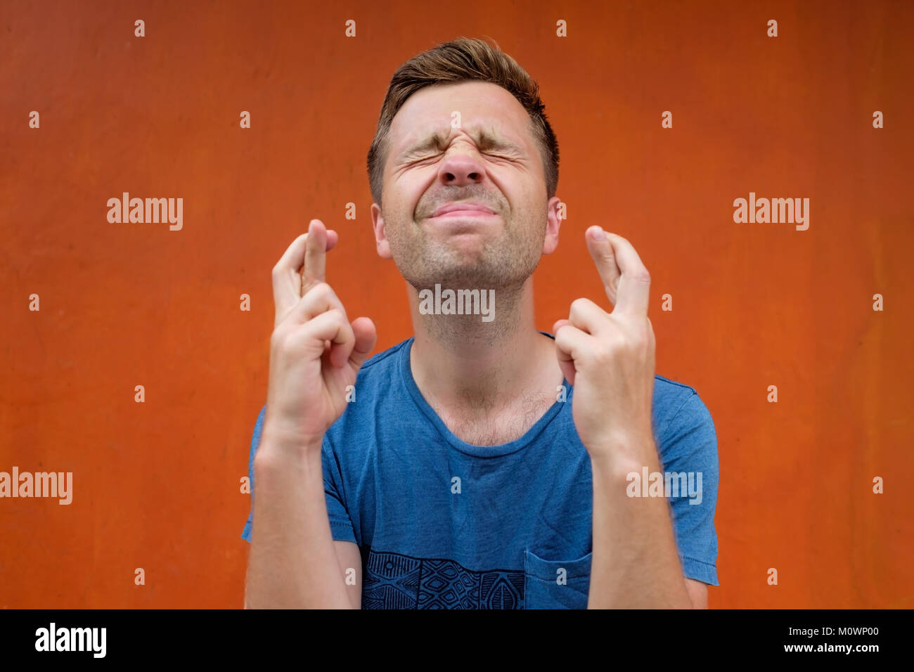 Young caucasian man making a wish isolated on red background. Concept ...