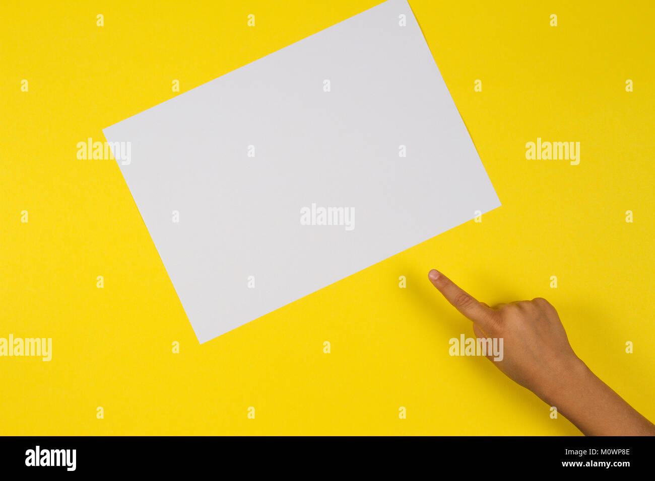 Kids hand finger pointing to white blank paper card on yellow ...