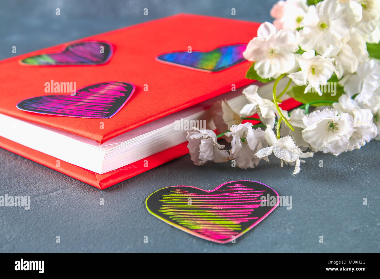 Black and pink hearts on a book in a red cover and flowers on a gray ...