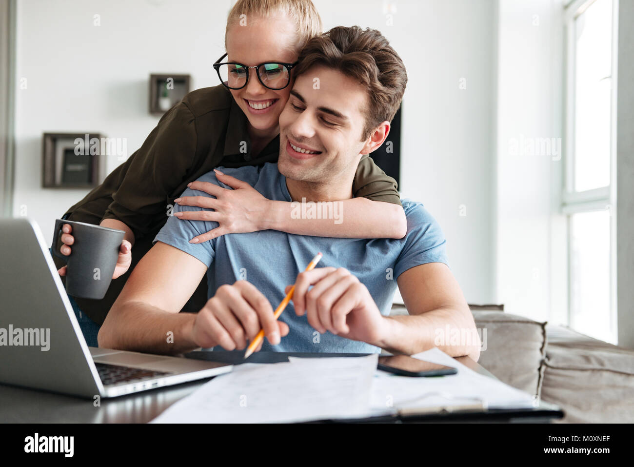 Smiling lady in glasses using laptop computer and hugging her ...