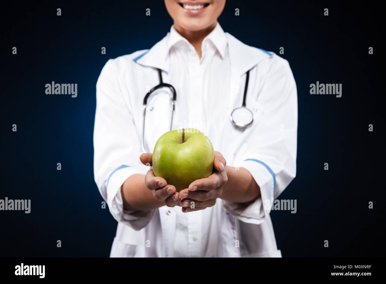 Cropped photo of young woman nurse in medical gown holding green apple ...