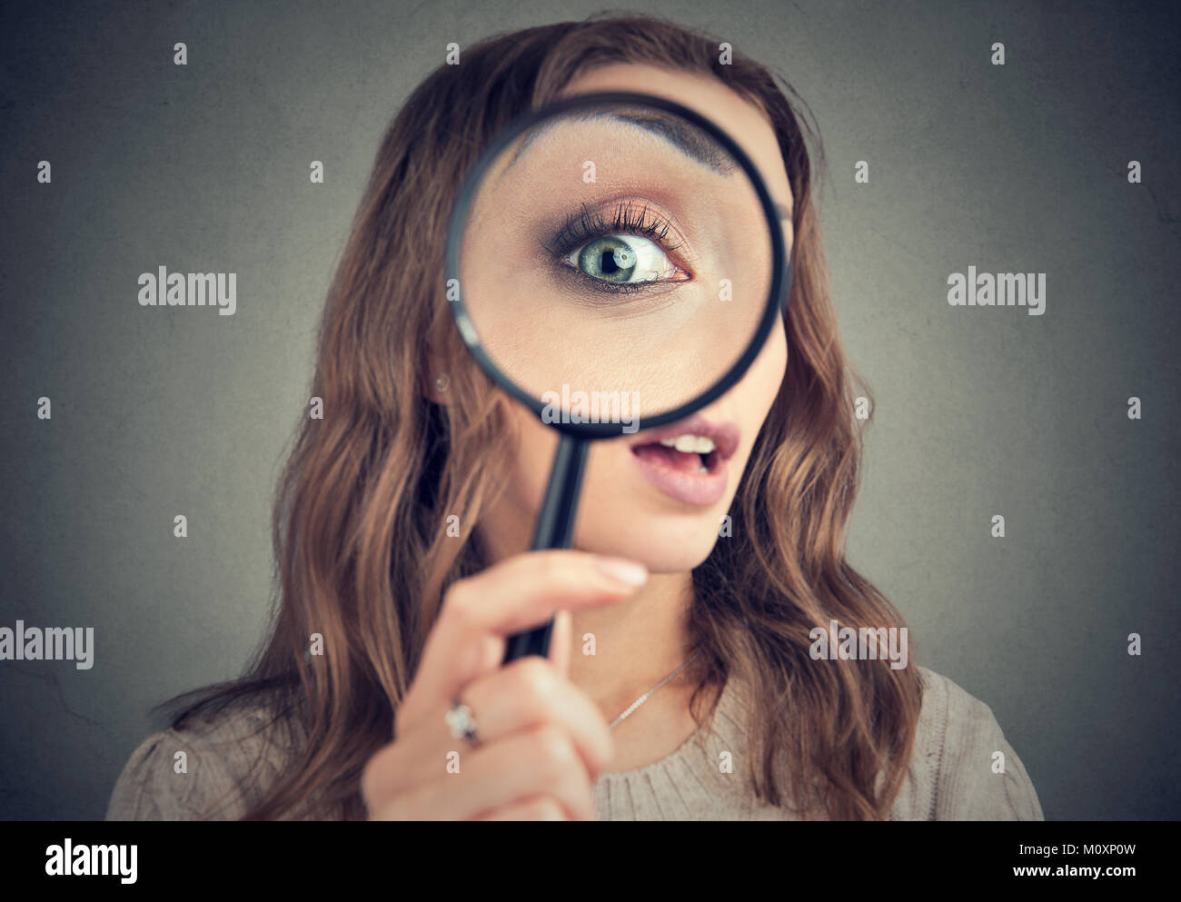 Young curious woman looking at camera through magnifying lens posing on ...