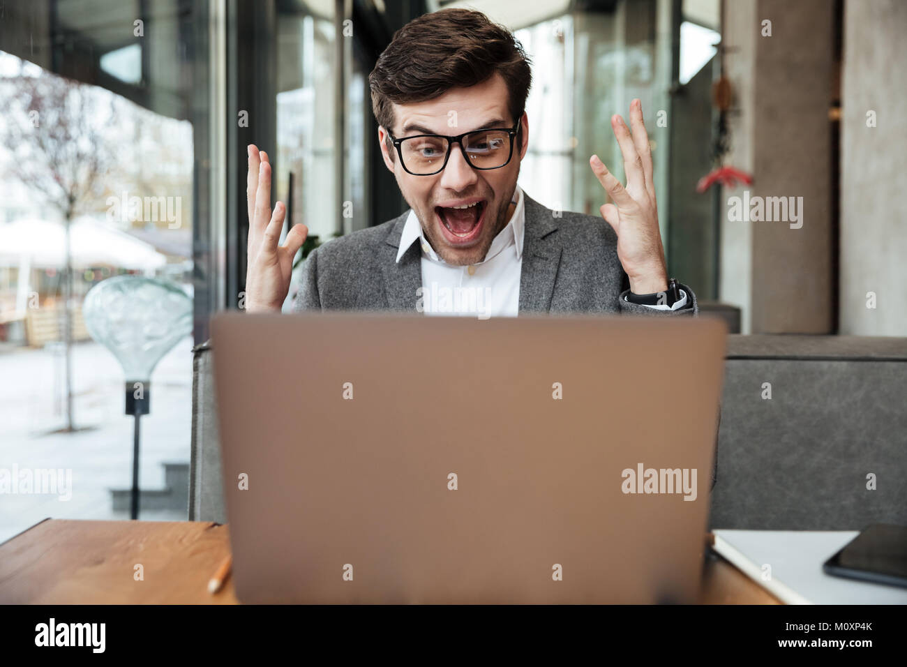 Shocked screaming business man in eyeglasses sitting by the table in ...