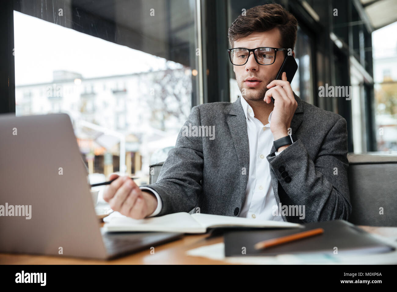 Confused business man in eyeglasses sitting by the table in cafe with ...