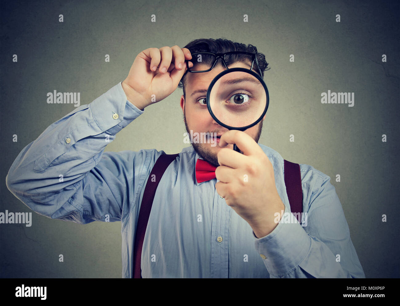Young chubby man looking at camera curiously through lens of magnifier ...