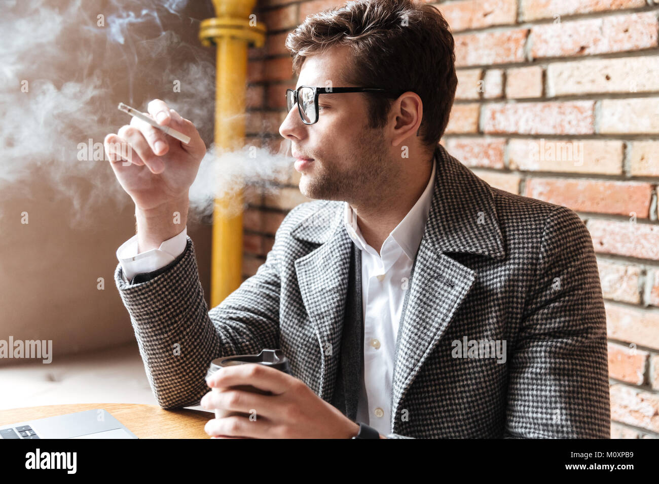Side view of handsome business man in eyeglasses sitting by the table ...
